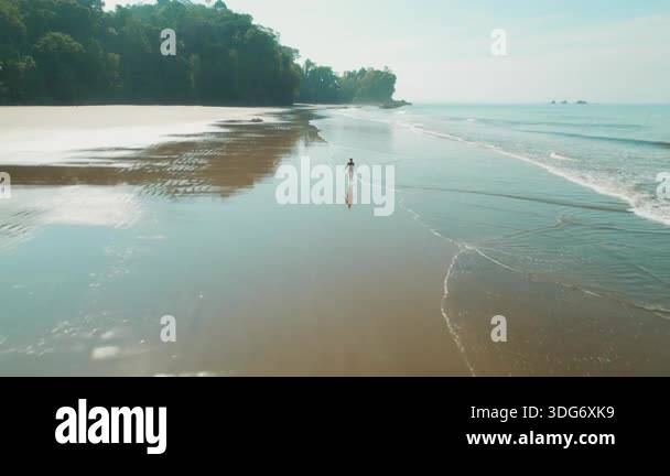 Woman in bikini running on sandy tropical beach near forest and calm ...