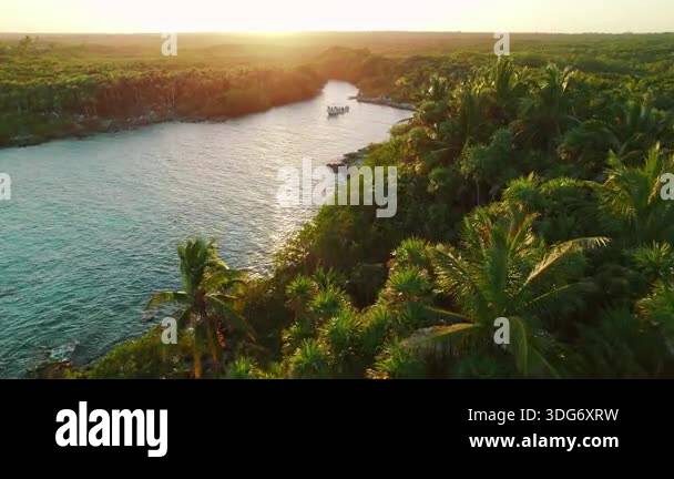 Boat sailing through tropical river surrounded by lush forest at golden ...