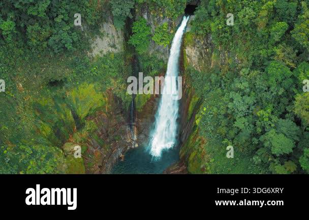 Waterfall exiting cave and flowing into deep pool in tropical forest ...