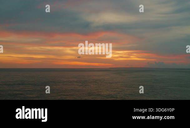 Colorful dramatic sunset over ocean horizon with dark clouds and smooth ...