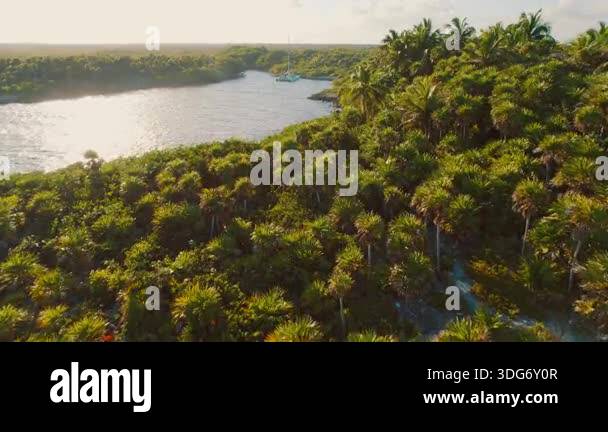 Sailboat anchored in calm tropical bay surrounded by lush jungle at ...
