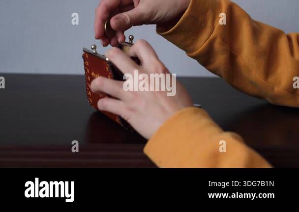 A person sits at a table and carefully opens a small coin purse. They ...