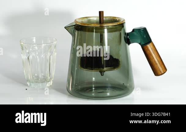 Making hot tea in an old transparent glass teapot on white background ...