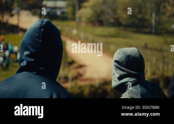 Rear view of two spectators in hoodies watching a rally car on a rural ...