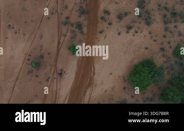 Top-down aerial view of an off-road motorcyclist riding across sandy ...