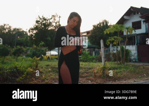 Attractive young asian woman in a black dress standing outdoors and ...