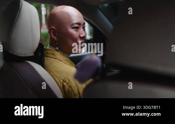 View from the back seat of a happy asian woman with a shaved head ...