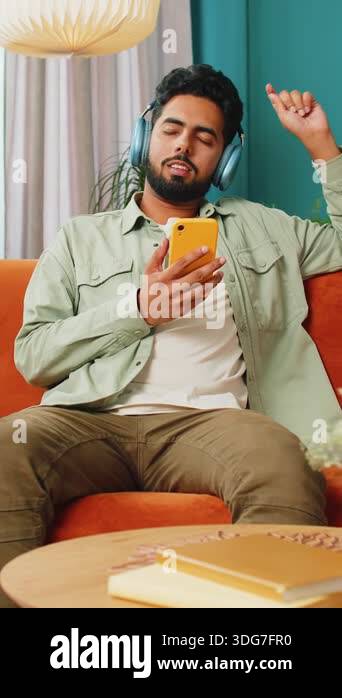 Happy relaxed overjoyed Indian man in wireless headphones dancing on ...