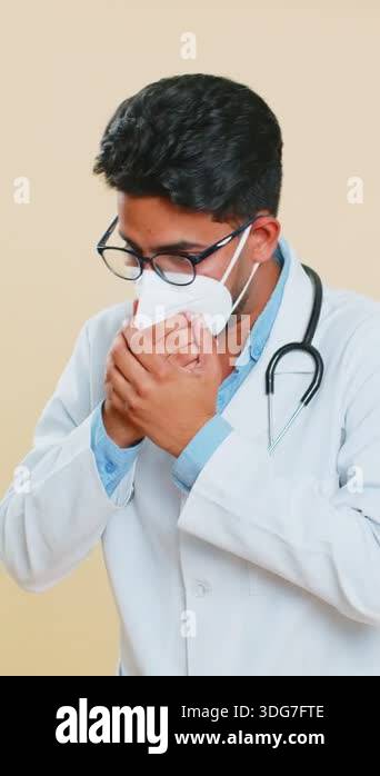 Unhealthy Indian young doctor man in protective mask coughing with ...