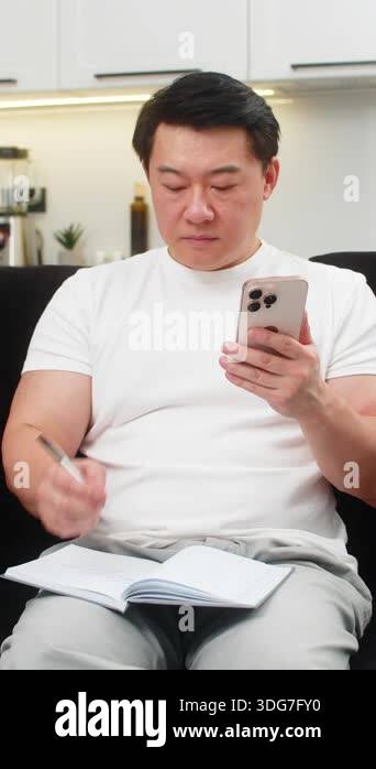 Asian man at home checks budget on smartphone calculator writes plans ...