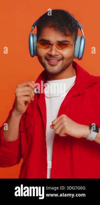 Happy stylish Indian man in sunglasses listening music via headphones ...