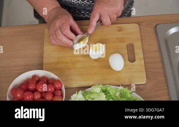 Cutting boiled egg into halves on wooden board for Caesar salad ...