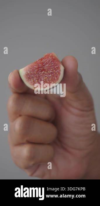 A person shows a half cut fig in hand. The fig appears fresh and ripe ...