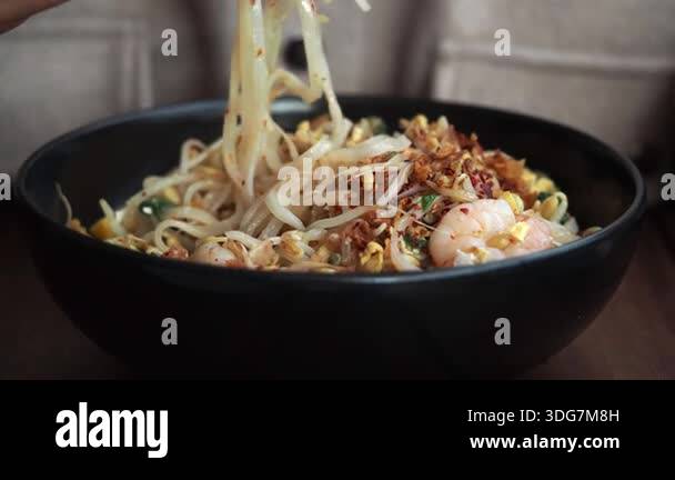 Person is eating a bowl of noodles with shrimp and vegetables using ...