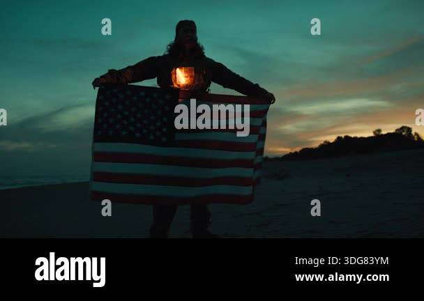 American flag wrapped around a soldier in silhouette at sunset night ...