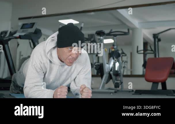 A man engages in a plank exercise on a gym mat. He wears a sweatshirt ...
