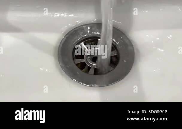 A close-up view of a white ceramic sink. Water is flowing directly into ...
