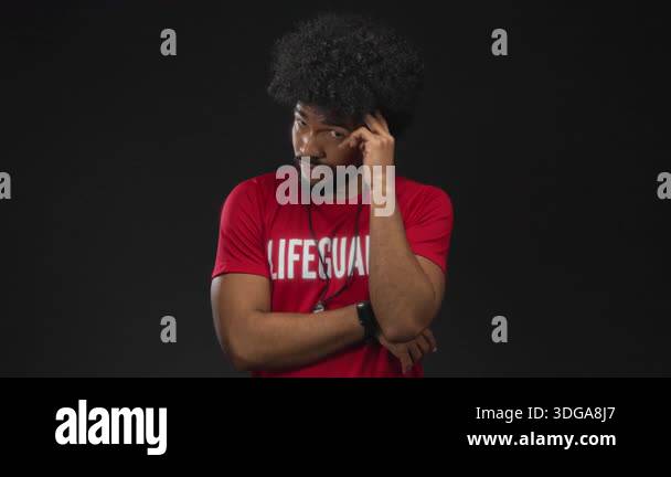Lifeguard man ponders against an isolated black background, wearing a ...