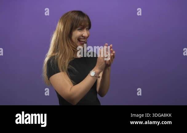 Woman clapping hands in purple studio, smiling and wearing a wristwatch ...