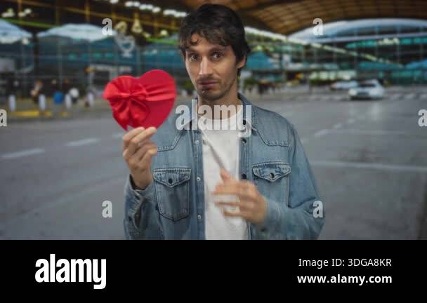 Man holds red heart box and points finger to head at busy airport ...