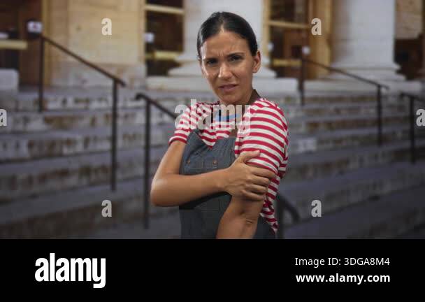 Woman holds her forearm on sunlit stone building steps wearing denim ...