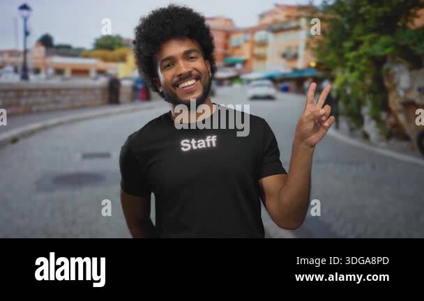 Smiling man in staff shirt making peace sign on city street outdoor ...