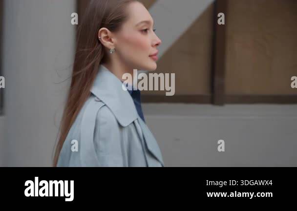 Side view of young woman with long hair walking on city sidewalk in ...