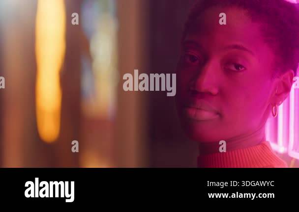 Smiling young Black woman standing beside glowing neon lights on city ...