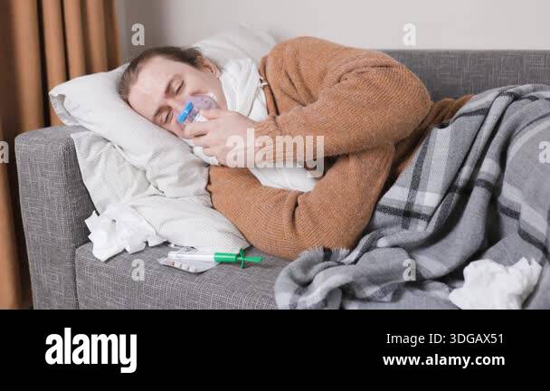 Sick man lying on a sofa finishing nebulizer inhalation therapy ...