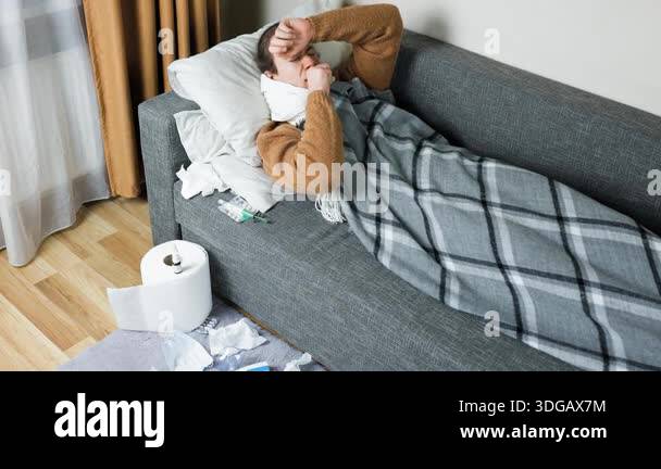 Sick man with flu symptoms lying on a sofa uses a nebulizer inhaler ...
