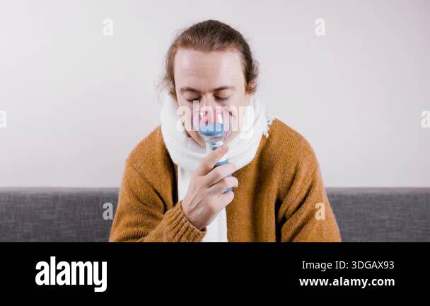Sick man with a red nose wearing a warm scarf and sweater uses a ...