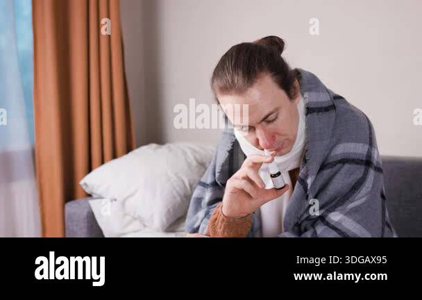 Sick man wrapped in a warm blanket using nasal spray to treat a runny ...