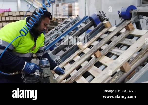Carpenter uses pneumatic nail gun to assemble wooden pallets in a ...