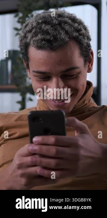 Happy young man smiling while texting on his mobile phone at home ...