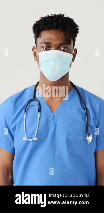 Vertical video of a young African American doctor in scrubs taking off ...