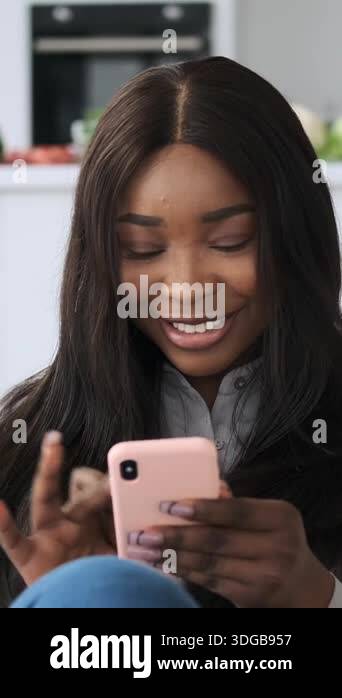 A young African American woman smiles while texting on her mobile phone ...