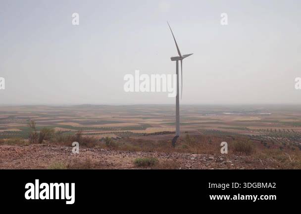A solitary wind turbine stands tall amidst an expansive rural landscape ...