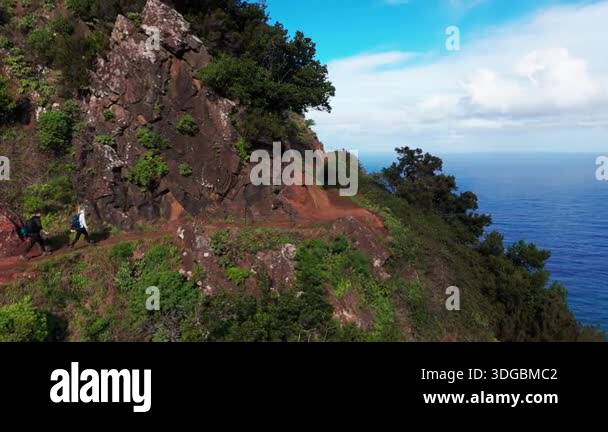 Coastal ridge trail with hikers navigating narrow dirt path along green ...