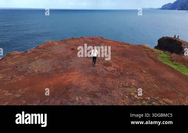 Solo traveler on red rocky plateau overlooking calm blue ocean ...