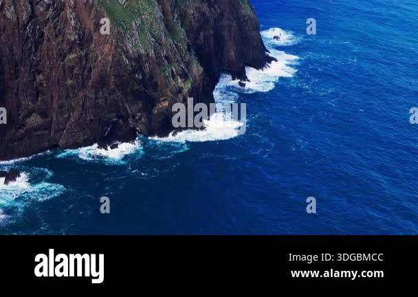 High vantage cliff face and deep blue ocean with crashing white surf ...
