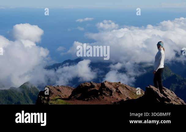 woman standing on rocky cliff edge with arms raised in triumph ...