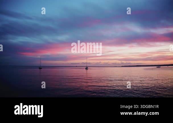 Wide shot of calm sea with sailboats anchored offshore beneath a ...