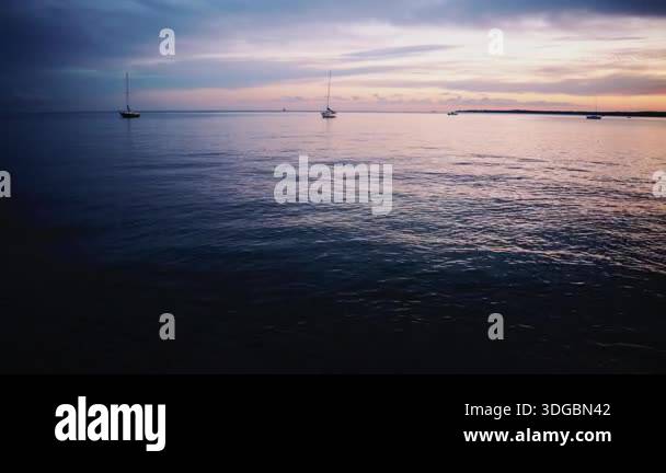 Wide shot of calm sea with sailboats anchored offshore beneath a ...
