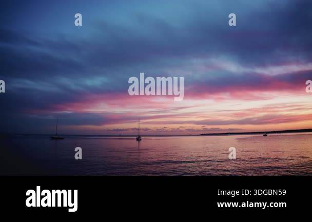 Wide shot of calm sea with sailboats anchored offshore beneath a ...
