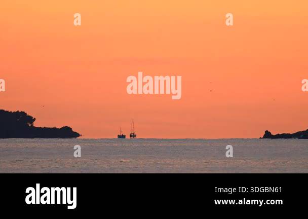 Wide shot of calm sea under a colorful sunset sky, with distant islands ...