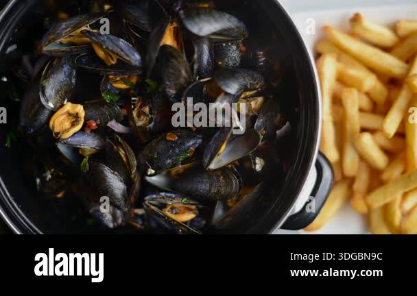 Cooked mussels served in a pot with herbs and sauce, accompanied by ...