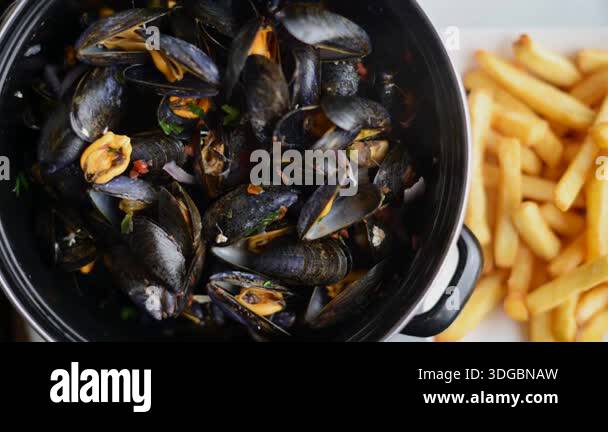 Cooked mussels served in a pot with herbs and sauce, accompanied by ...