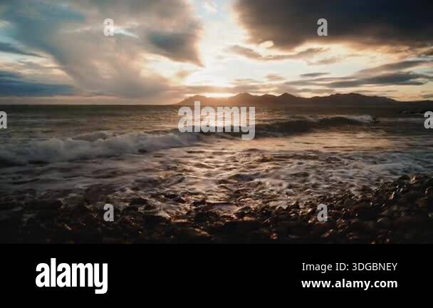 Evening waves washing over a rocky shoreline under dramatic clouds and ...