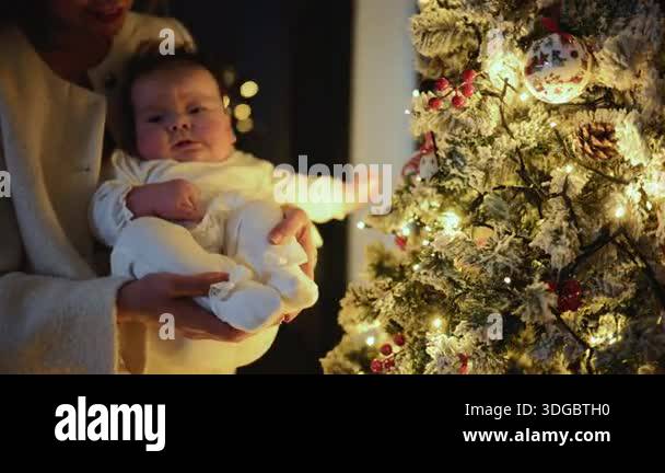 Happy mother holding a baby indoors next to a decorated Christmas tree ...