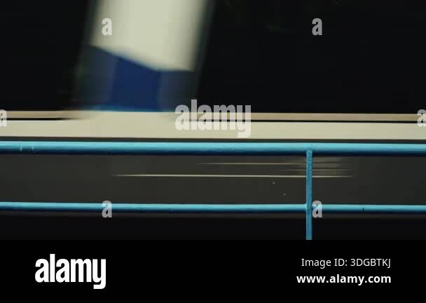 Side view of a passenger train moving past a blue fence near the ...